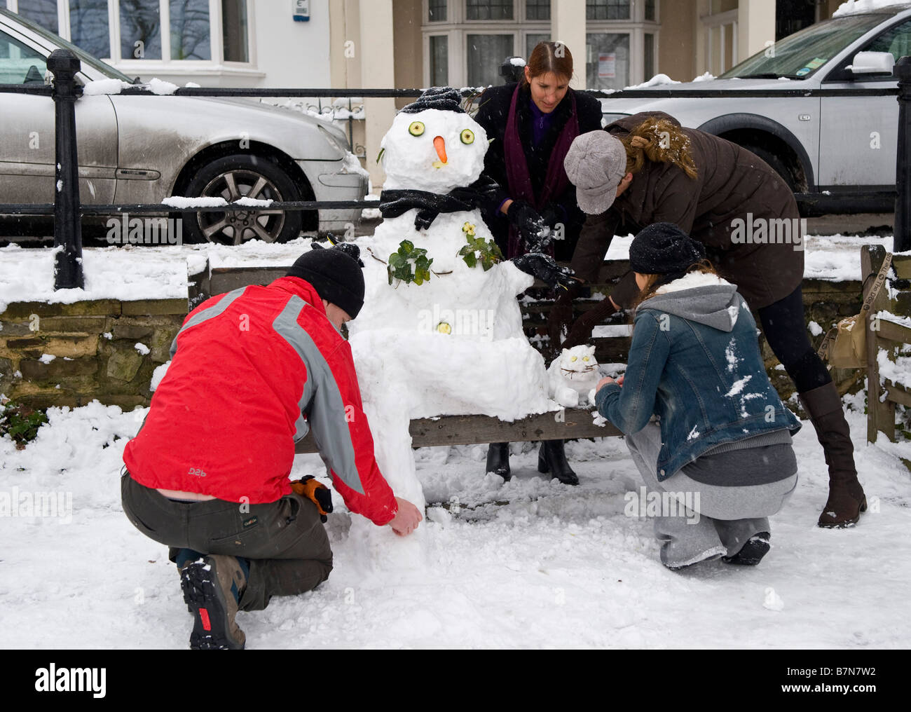 Finishing touches on a snowman and snowcat sitting on a park bench ...