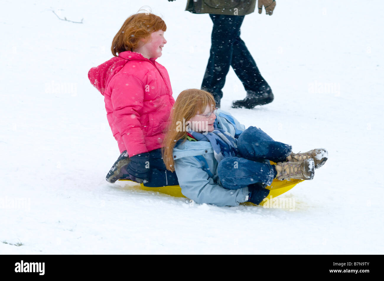 Two Girls Children riding on a sled sledge sledging in the Snow Stock ...
