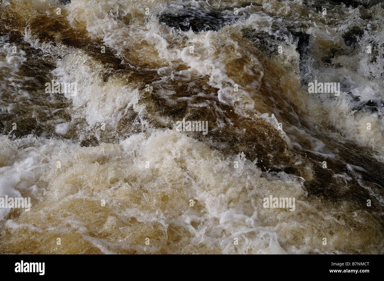Close up on fast running water with brown floodwater and white rapids ...