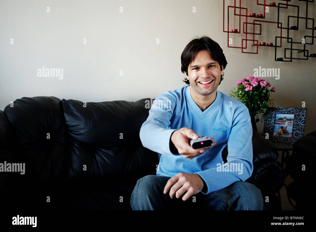 Young man holding a remote control sitting on a sofa Stock Photo - Alamy