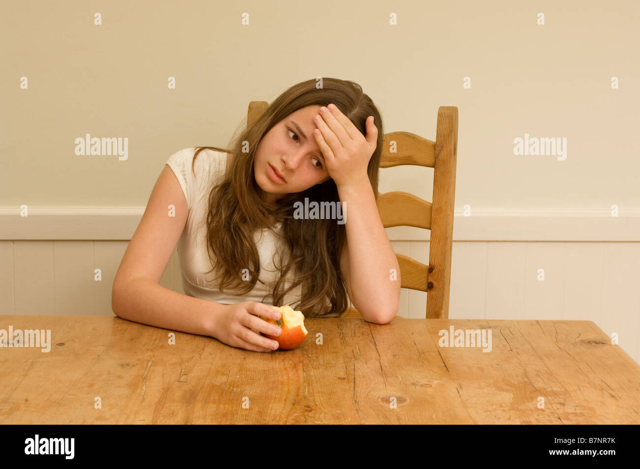 young girl sitting at table eating apple with hand on forehead Stock ...