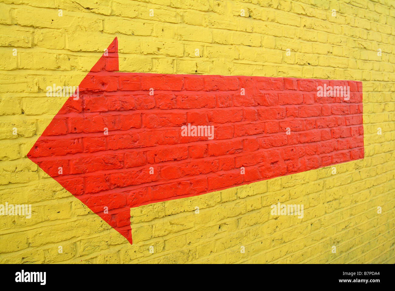 A large red arrow on a painted yellow brick wall Stock Photo - Alamy