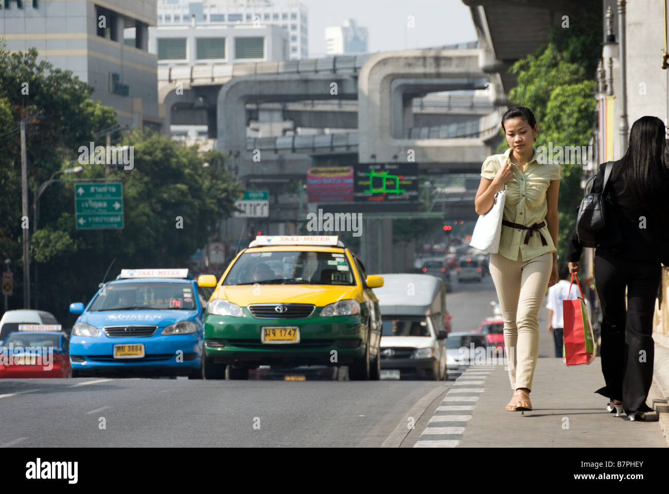 Pedestrians walking along busy main road with overhead metro ...