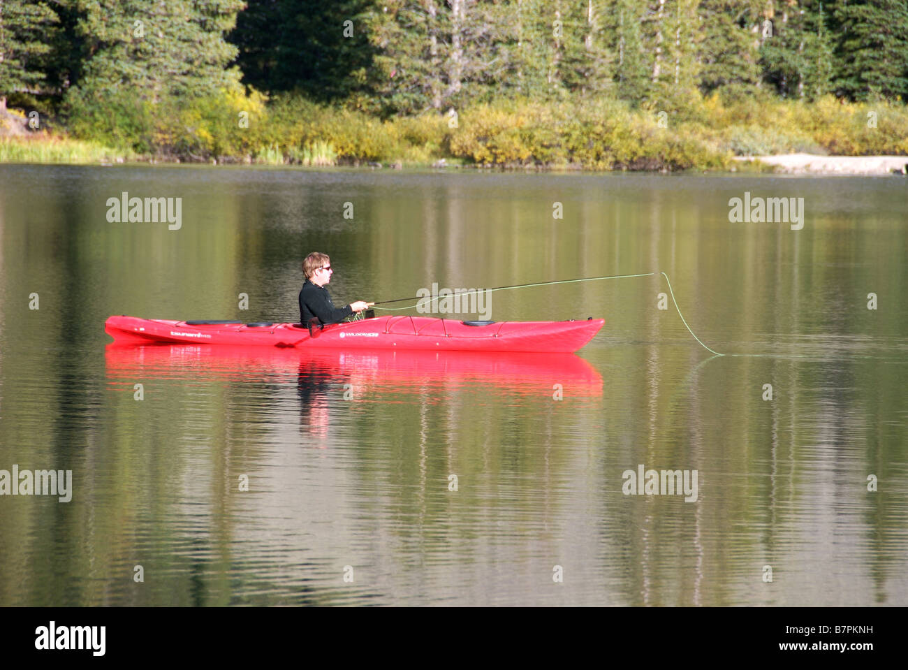 a man fly fishing from his kayak for rising trout high up in the san ...