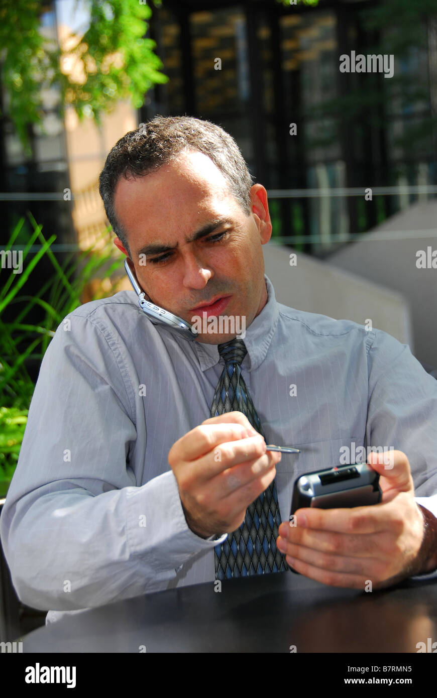Busy businessman talking on cell phone and working on his palm pilot ...