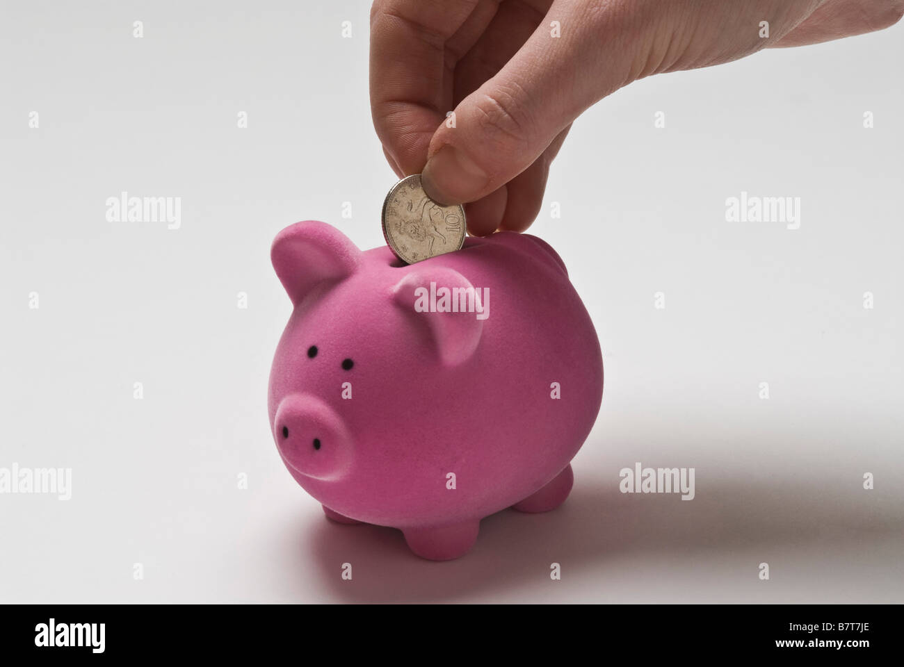 Inserting coin into a pink piggybank Stock Photo - Alamy