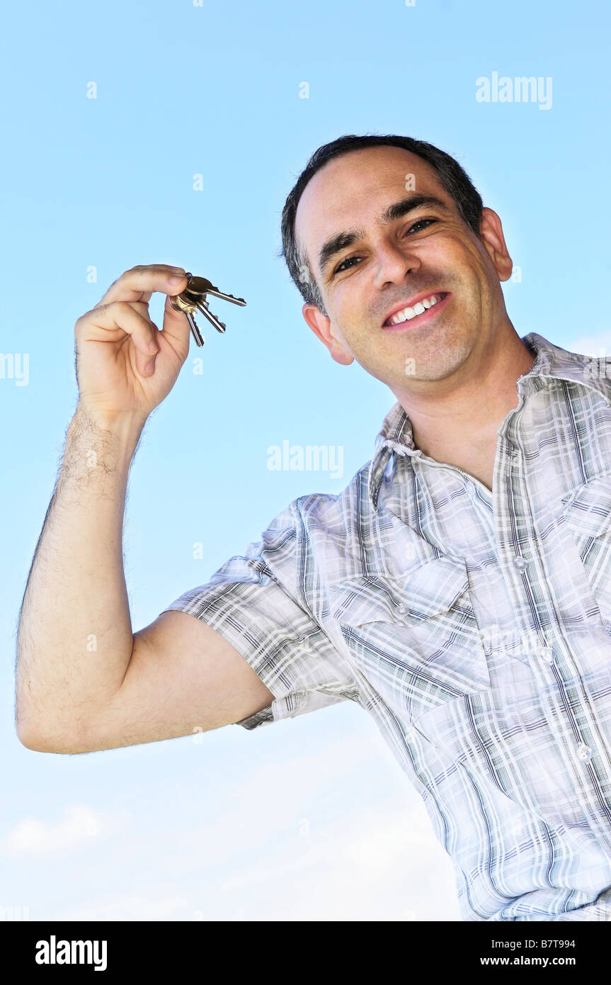 Smiling man holding house keys on blue sky background Stock Photo - Alamy