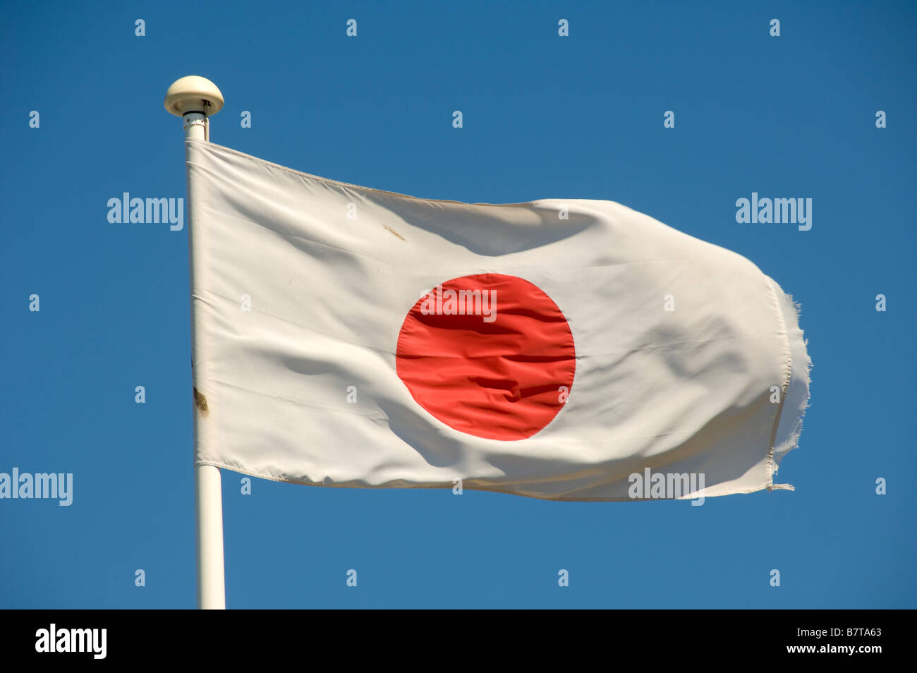 Japanese flag flying on a white flagpole seen against a blue sky Stock ...