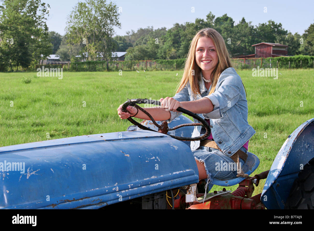 A beautiful farmer s daughter driving a tractor through a green field ...