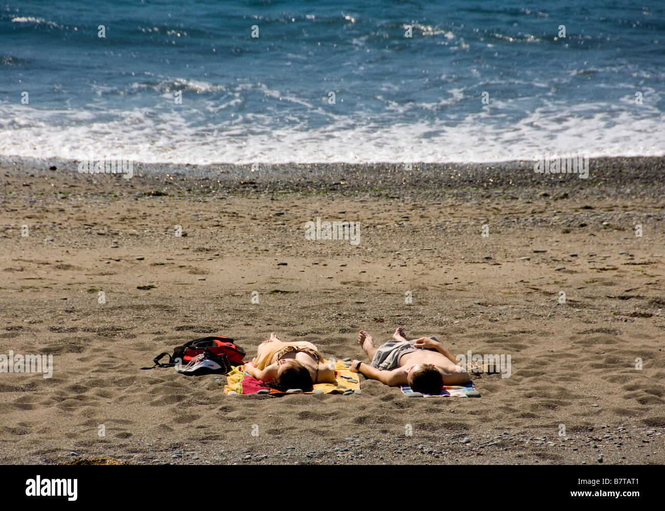Unidentifiable caucasian couple laid on towels sunbathing on beach with ... Unidentifiable caucasian couple laid on towels sunbathing on beach with ...