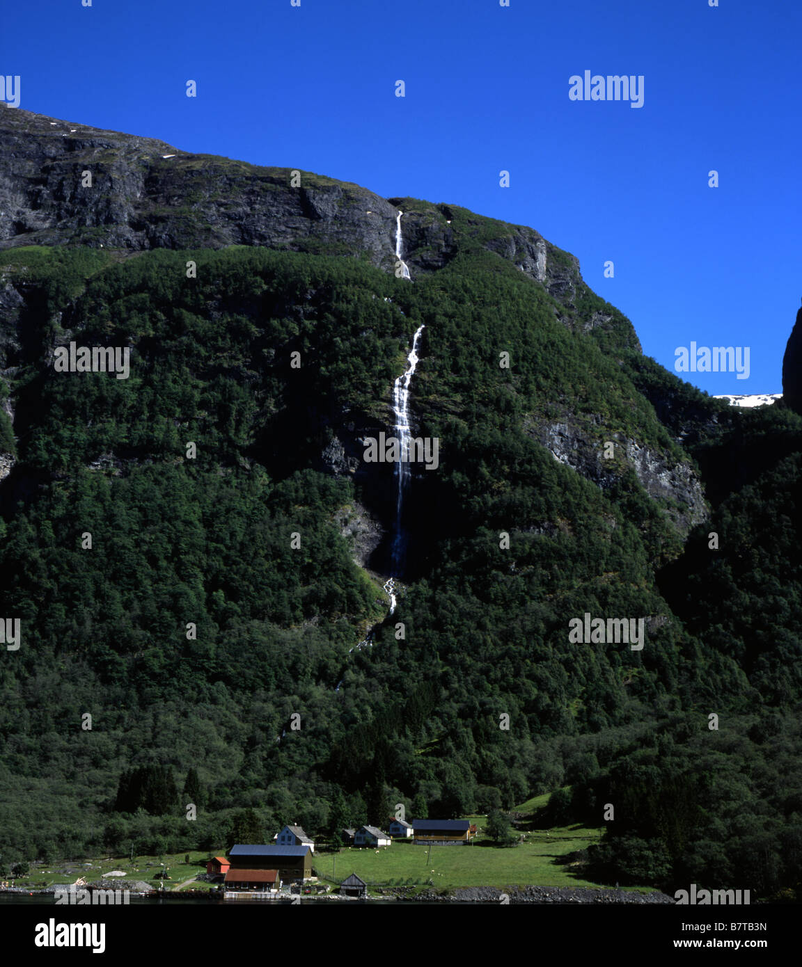 Small village and waterfall cascading down a wooded cliff ...