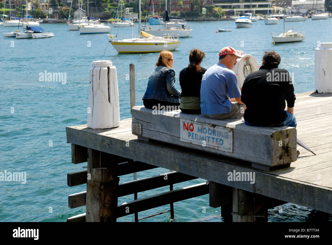 Group of people sitting on jetty, above a "No Mooring Permitted" sign ...