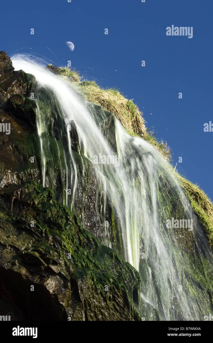 The moon rises over a cascading waterfall at Sandymouth beach, North ...