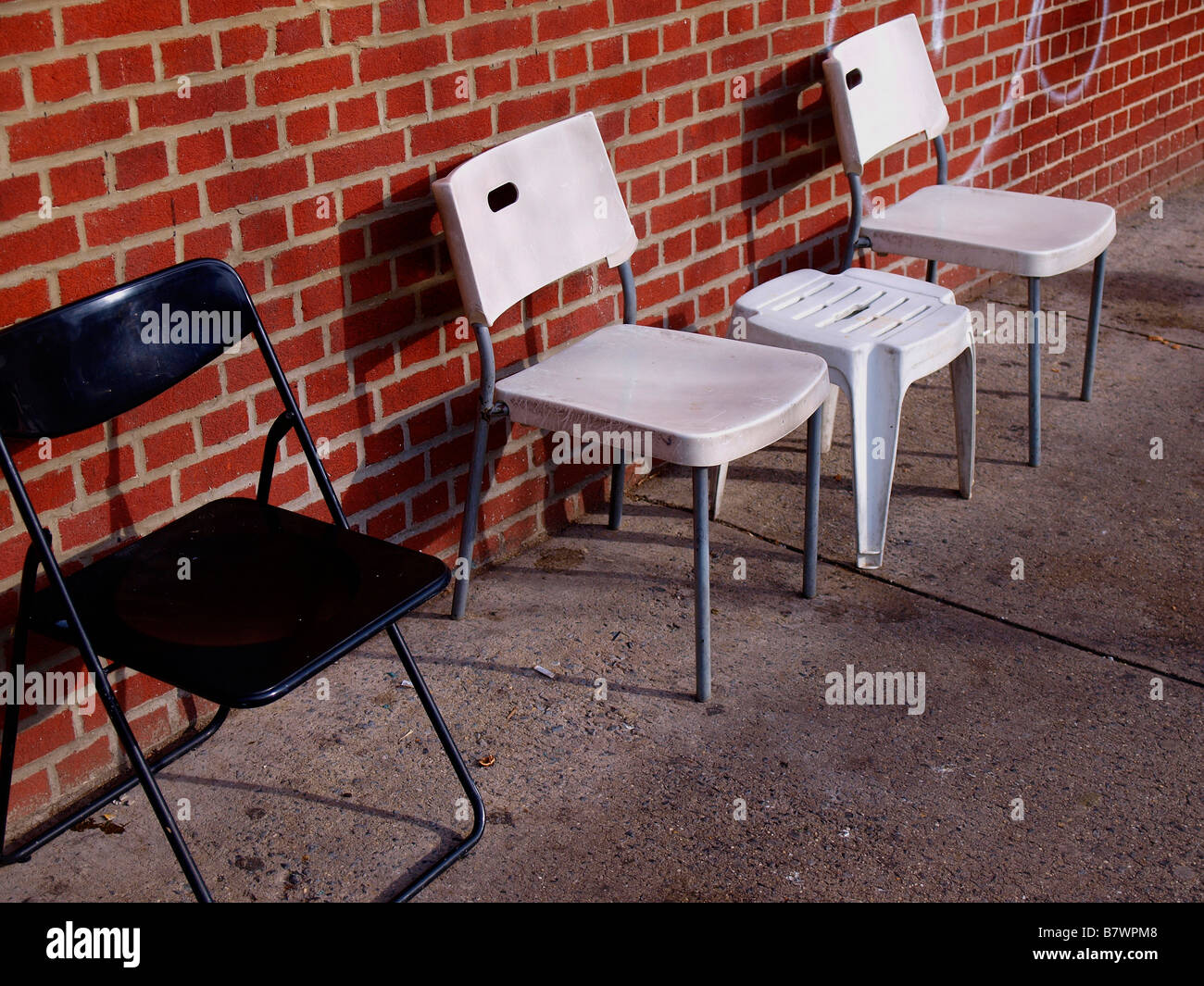 Plastic folding chairs of various styles on a city sidewalk against a ...