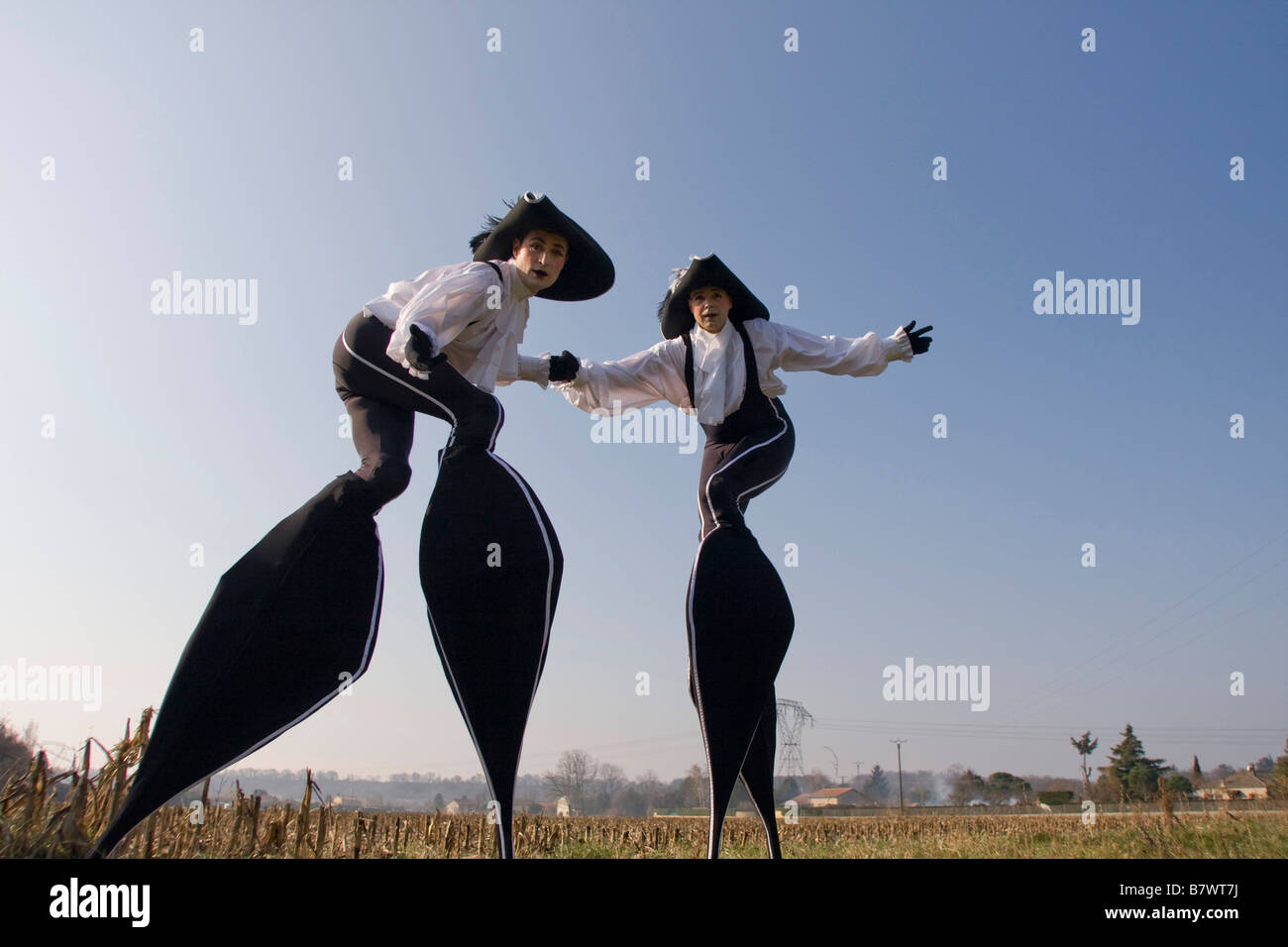 2 actors dressed in mousquetaire costume on tall stilts with black hat ...