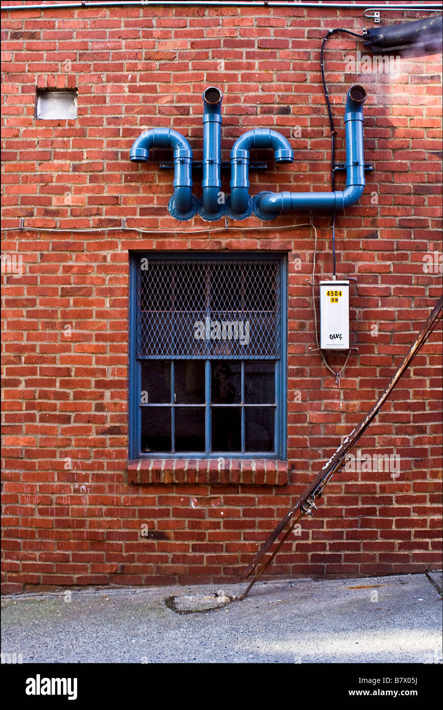 A brick wall with a window in it and blue pipes with steam coming out ...