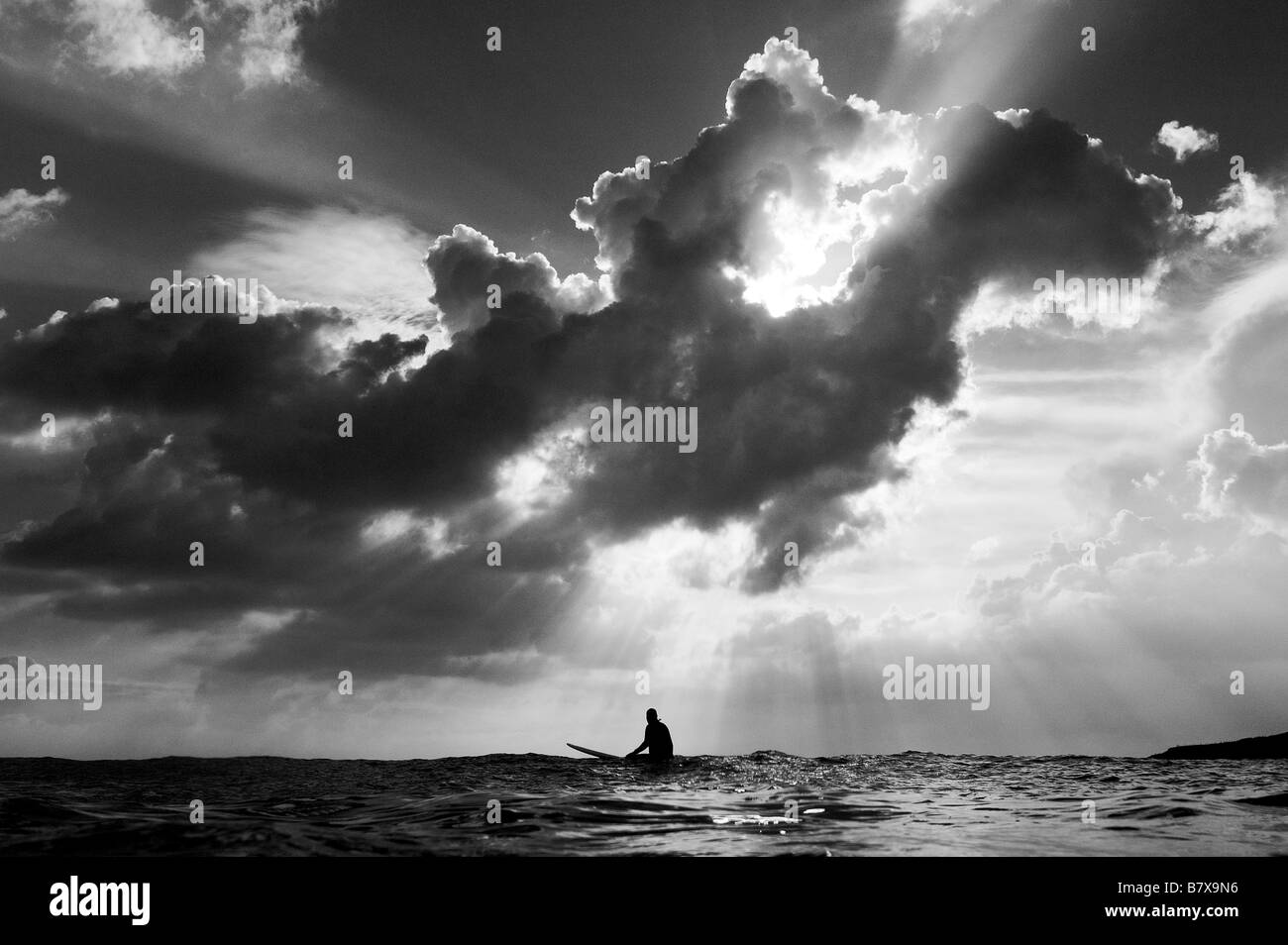 Lone surfer waits for the next wave as clouds draw shapes in the sky ...