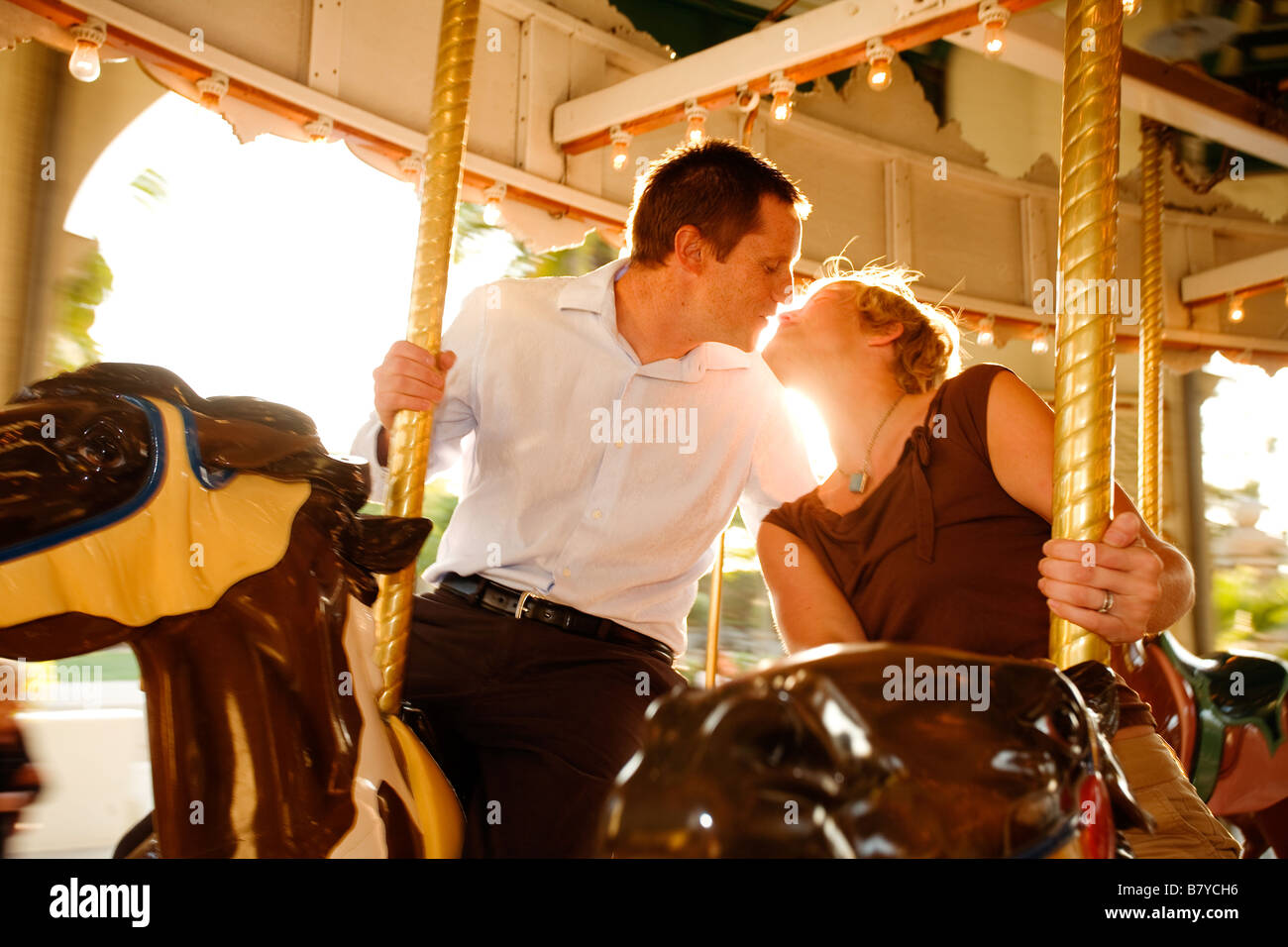 A romantic backlit couple kissing on a carousel in the warm light of ...