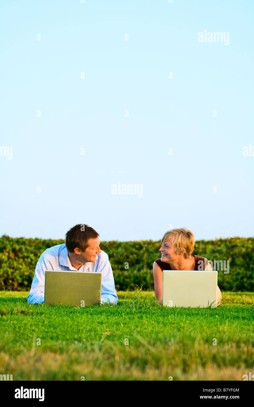 A modern couple remote working on a laptop computer outside in a park ...