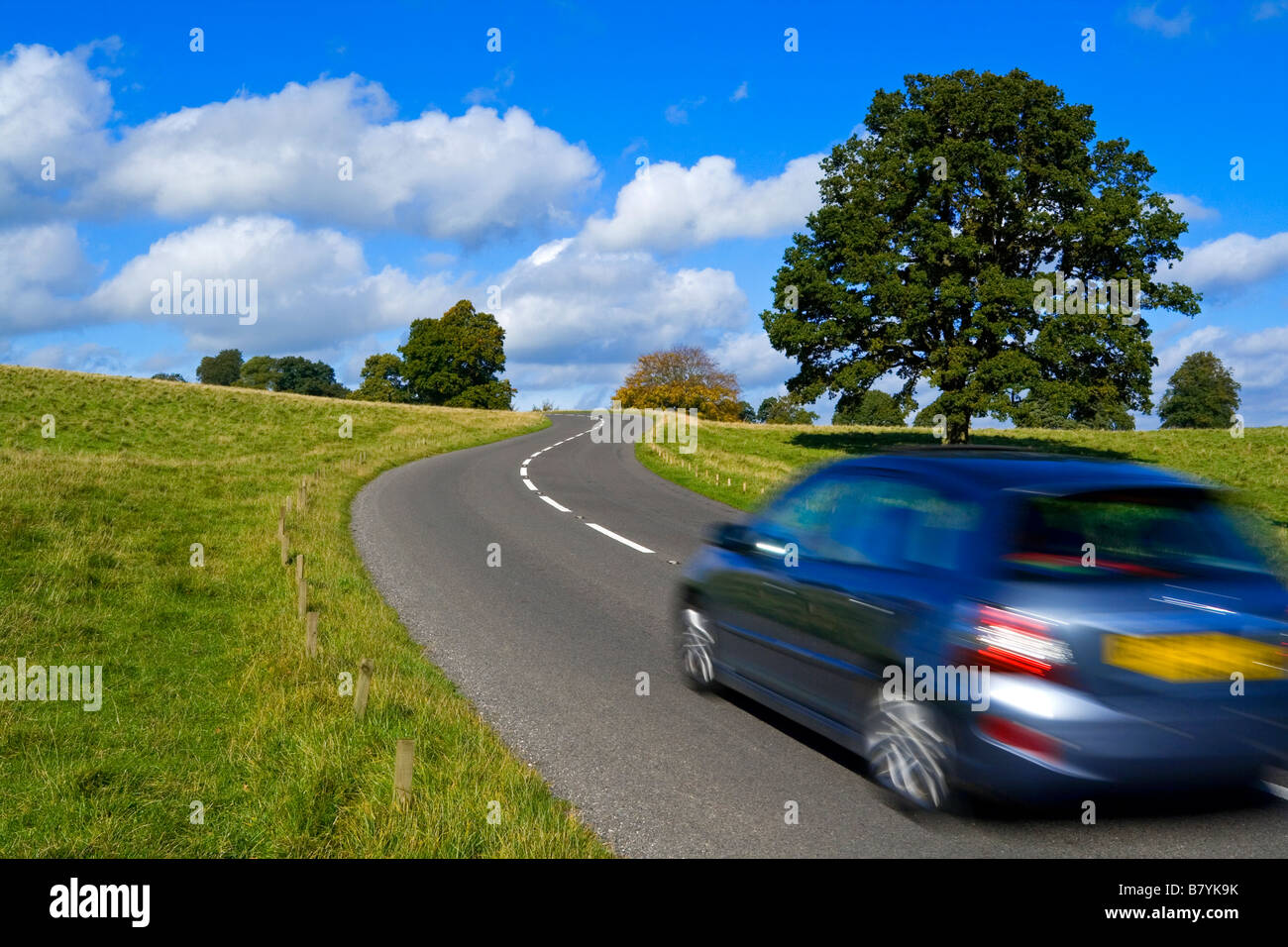 Car driving fast on a winding country road with trees and a cloudy blue ...