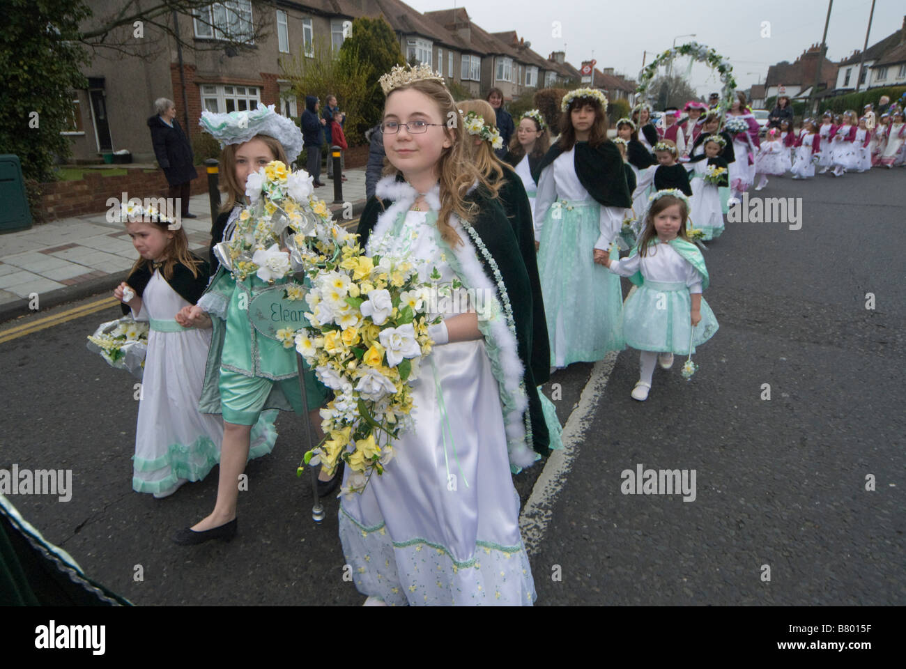 A May Queen with crown and holding flowers leads her retinue along a ...