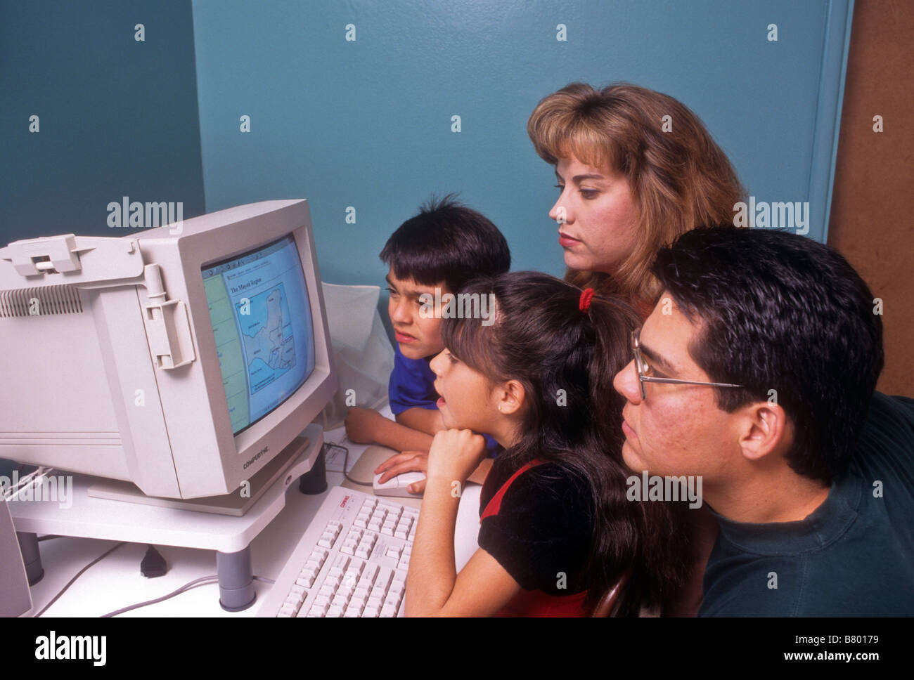 Parents help children work on early model home computer Stock Photo - Alamy