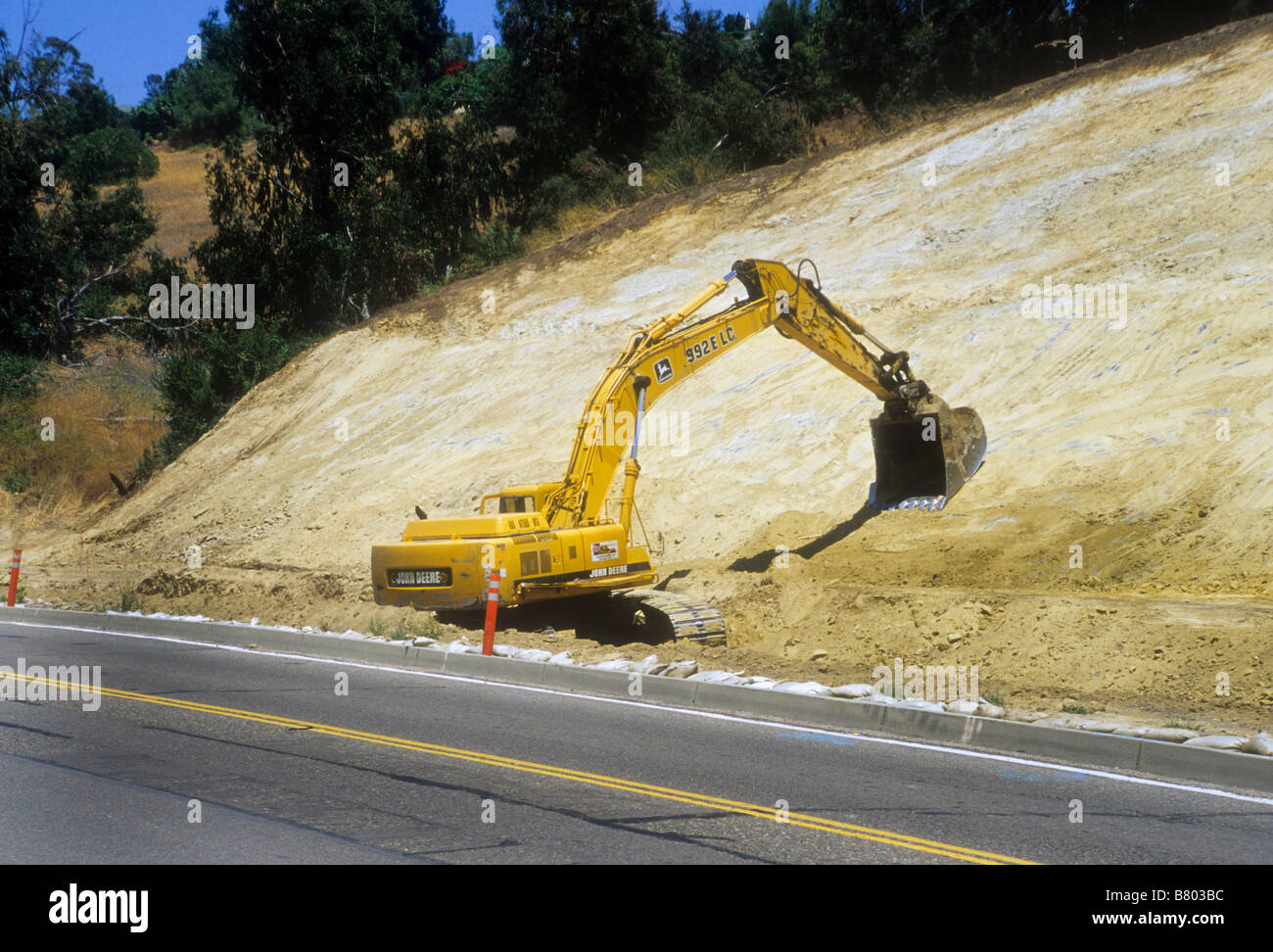 Large backhoe sculpts hillside in road project Stock Photo - Alamy