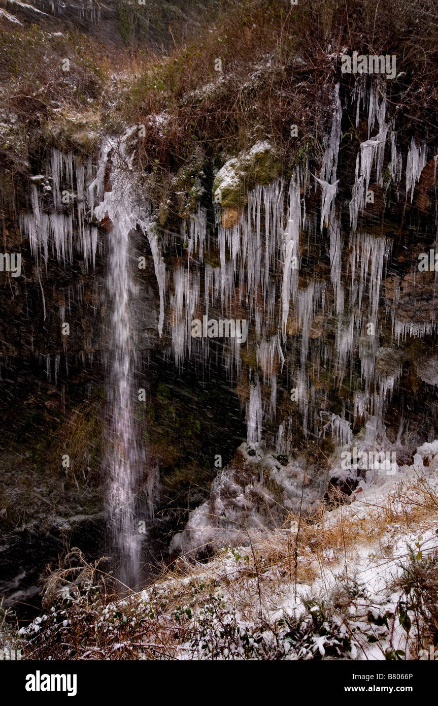 Snow flakes falling on a small waterfall as it flows through icicles ...