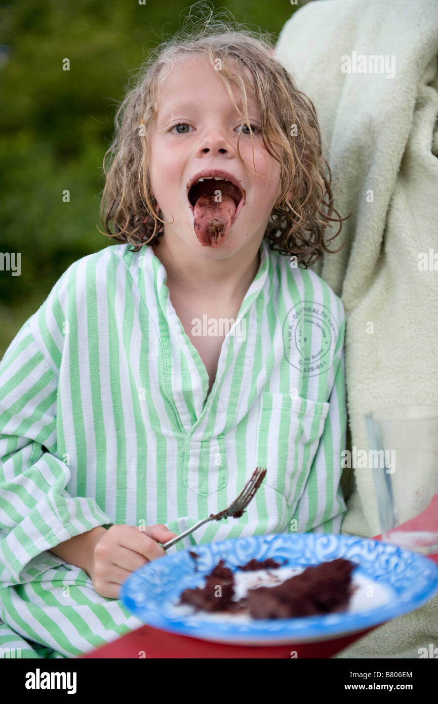 A young boy enjoying chocolate cake on a summers day at the cottage ...