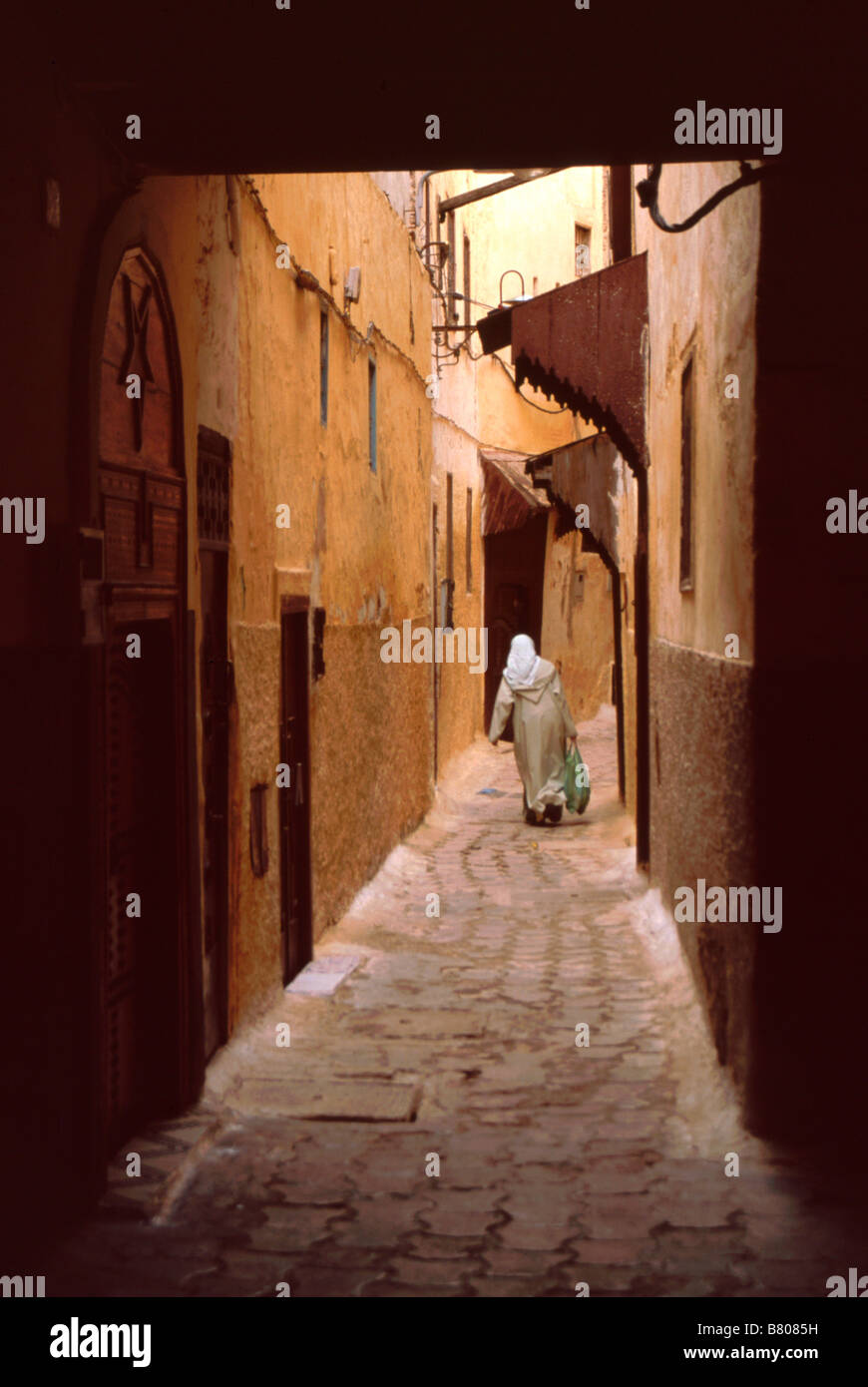 North African woman walks along narrow medina street fringed by high ...