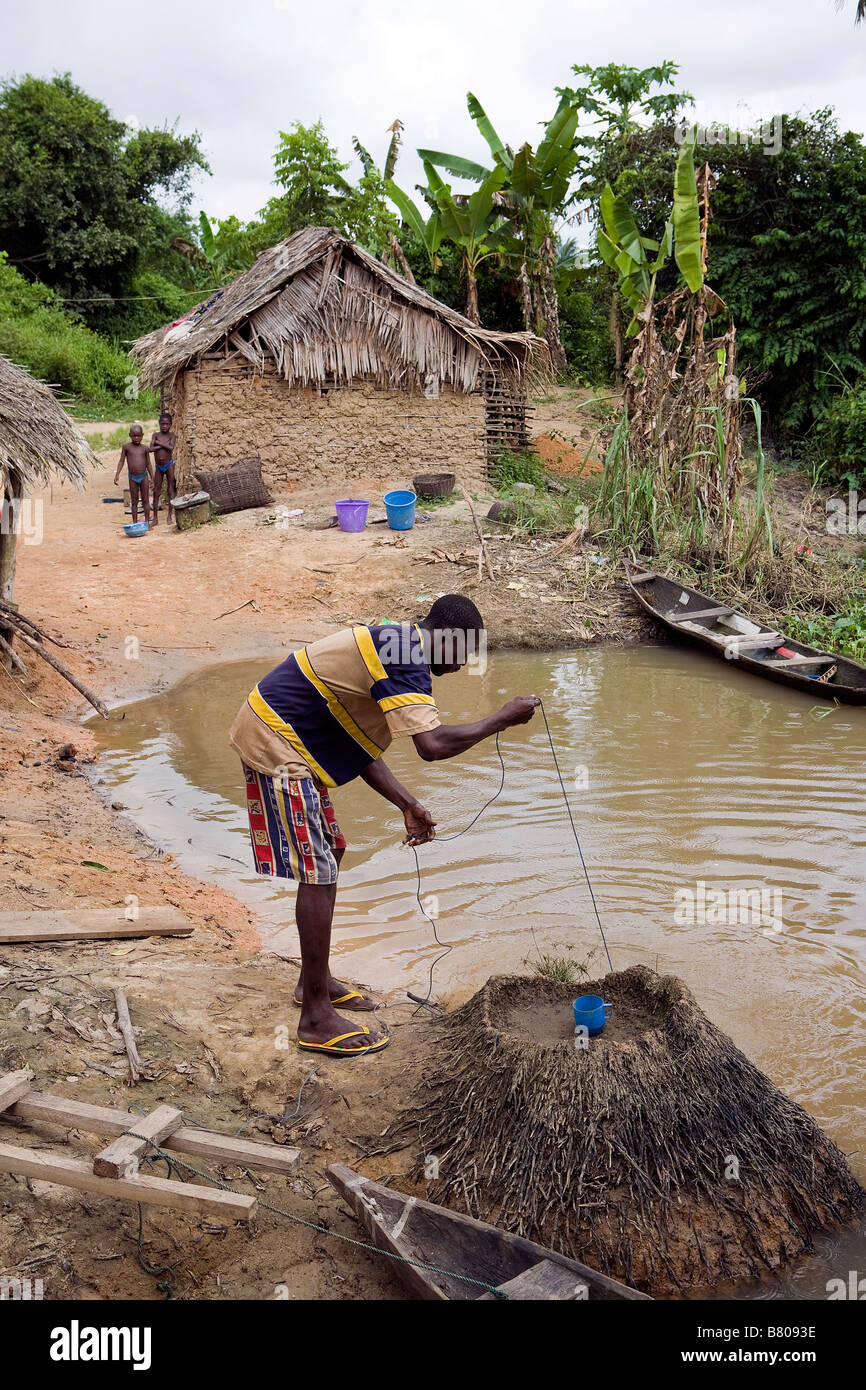A group of local kids watch a villager fish in a small water cove in a ...