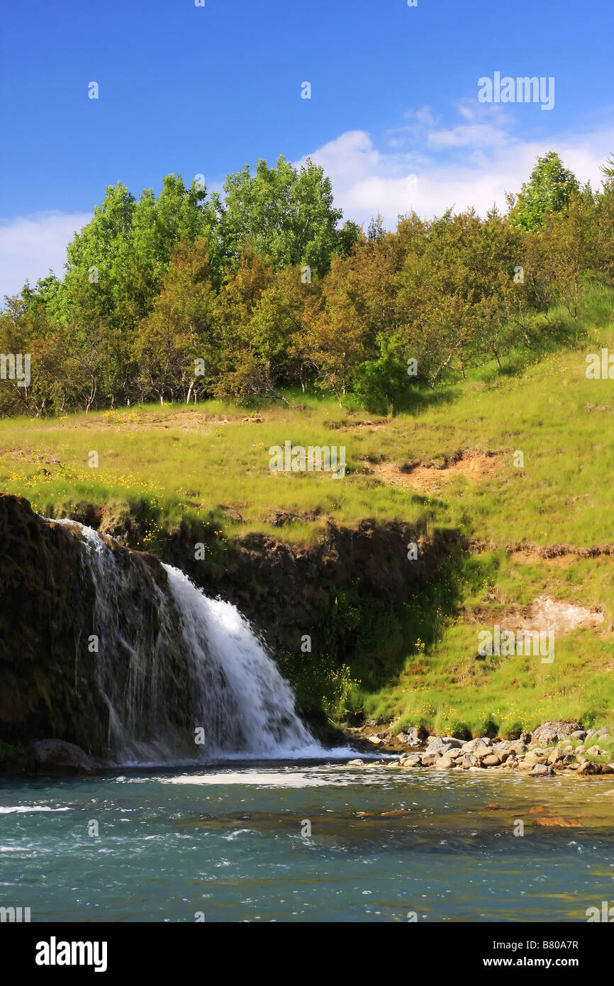 A small waterfall during summer set against gentle hills with small ...
