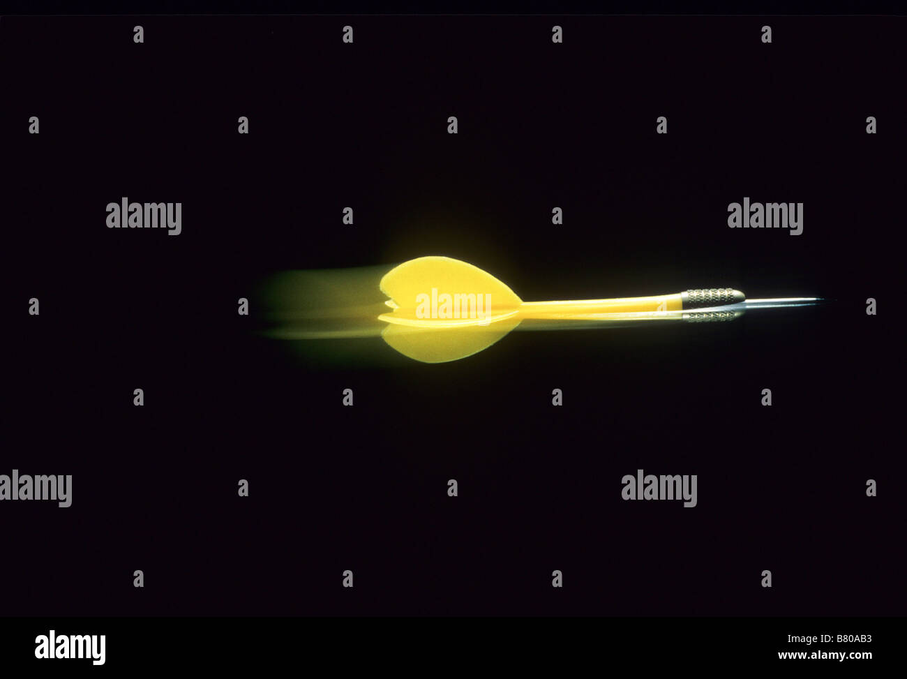Yellow dart flies through air in front of black background Stock Photo ...