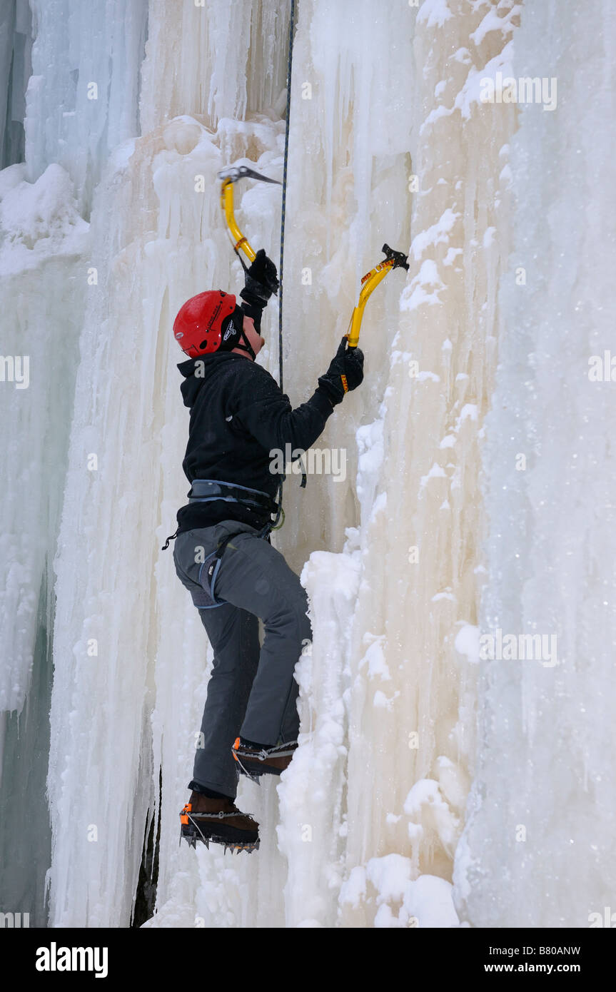 Single ice climber front pointing up sheer vertical wall of ice on ...