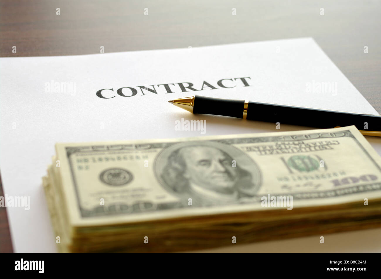 Contract page with pen and stack of dollars on table Stock Photo - Alamy
