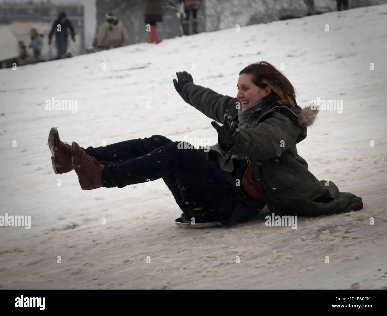 Smiling woman sliding down a snowy hill, Primrose Hill, London, England ...