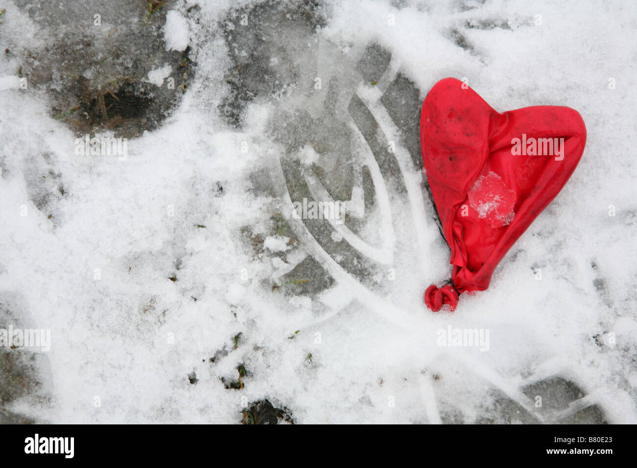 Deflated red heart-shaped balloon trampled in the snow Stock Photo - Alamy