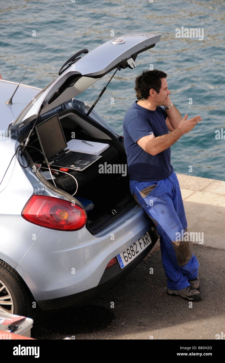Male service engineer using mobile phone and laptop computer situated ...