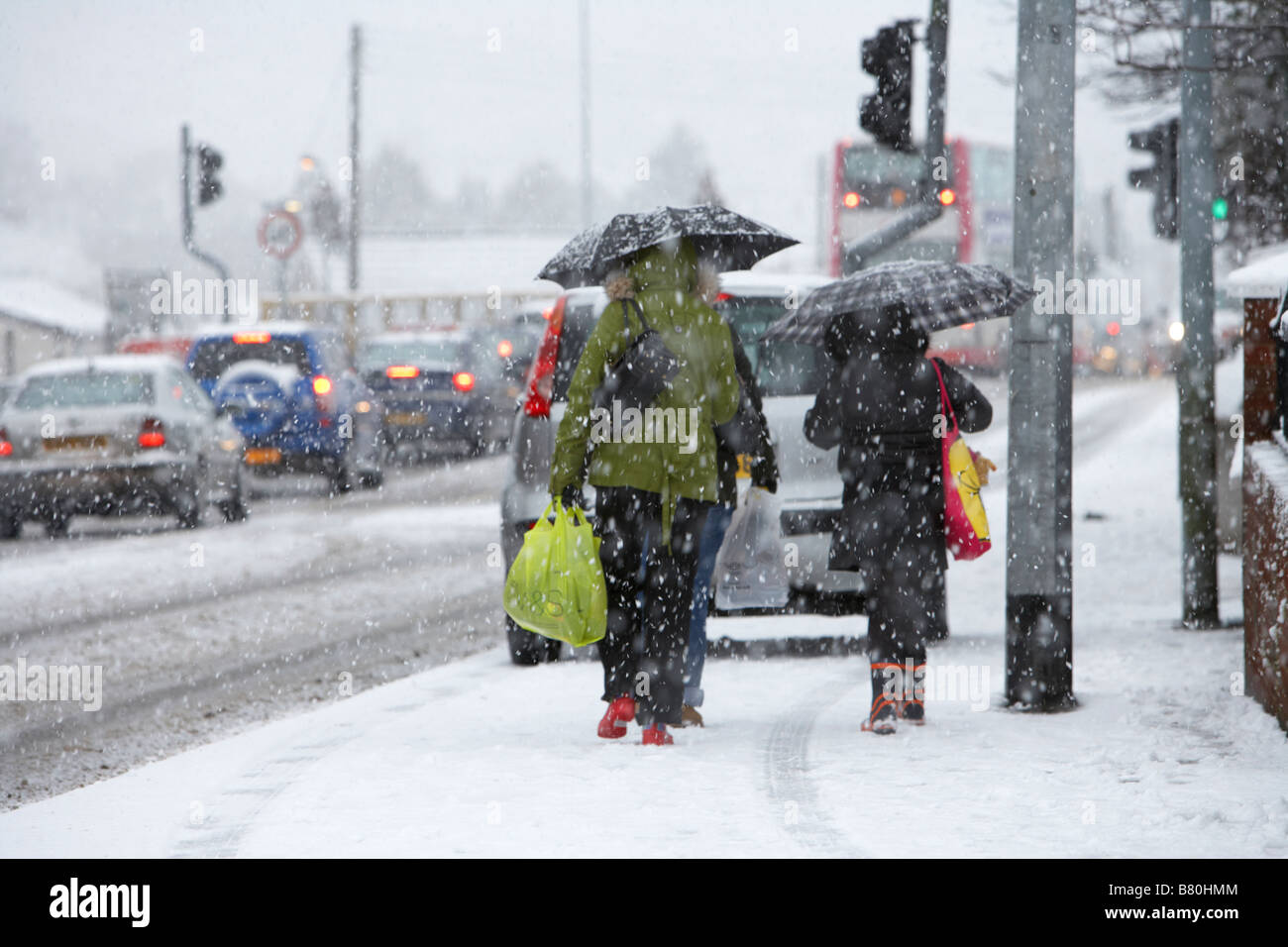 women walking along snow covered footpath past queue of traffic in ...