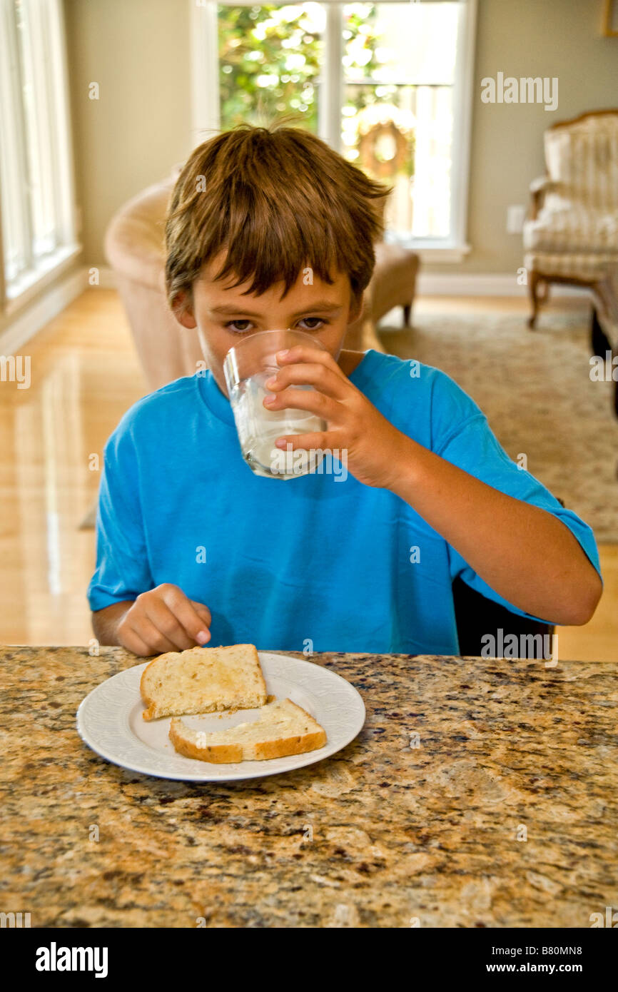 A 10 year old boy eats his breakfast of toast and milk at home in ...