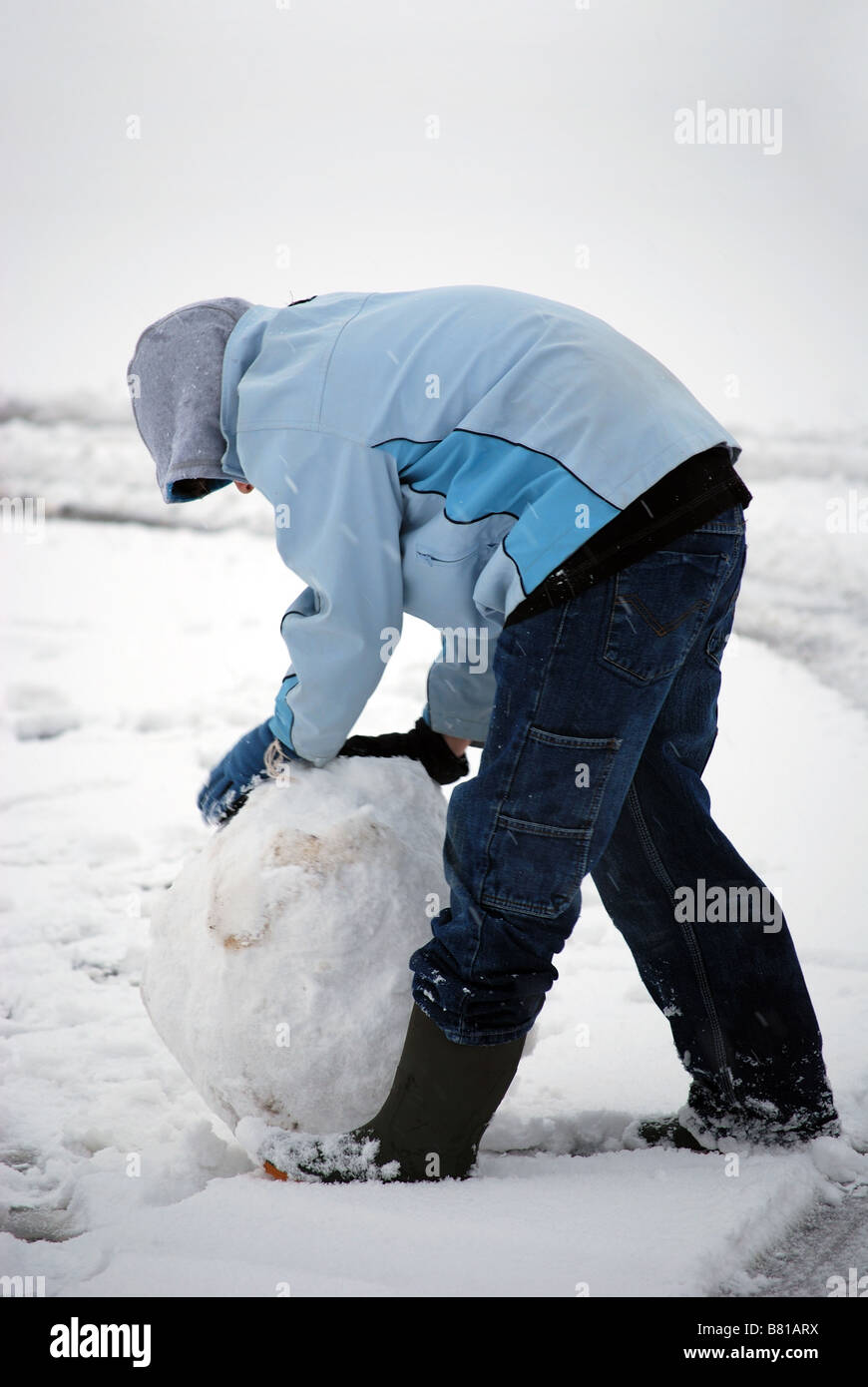 Boy rolling a large snowball Stock Photo - Alamy