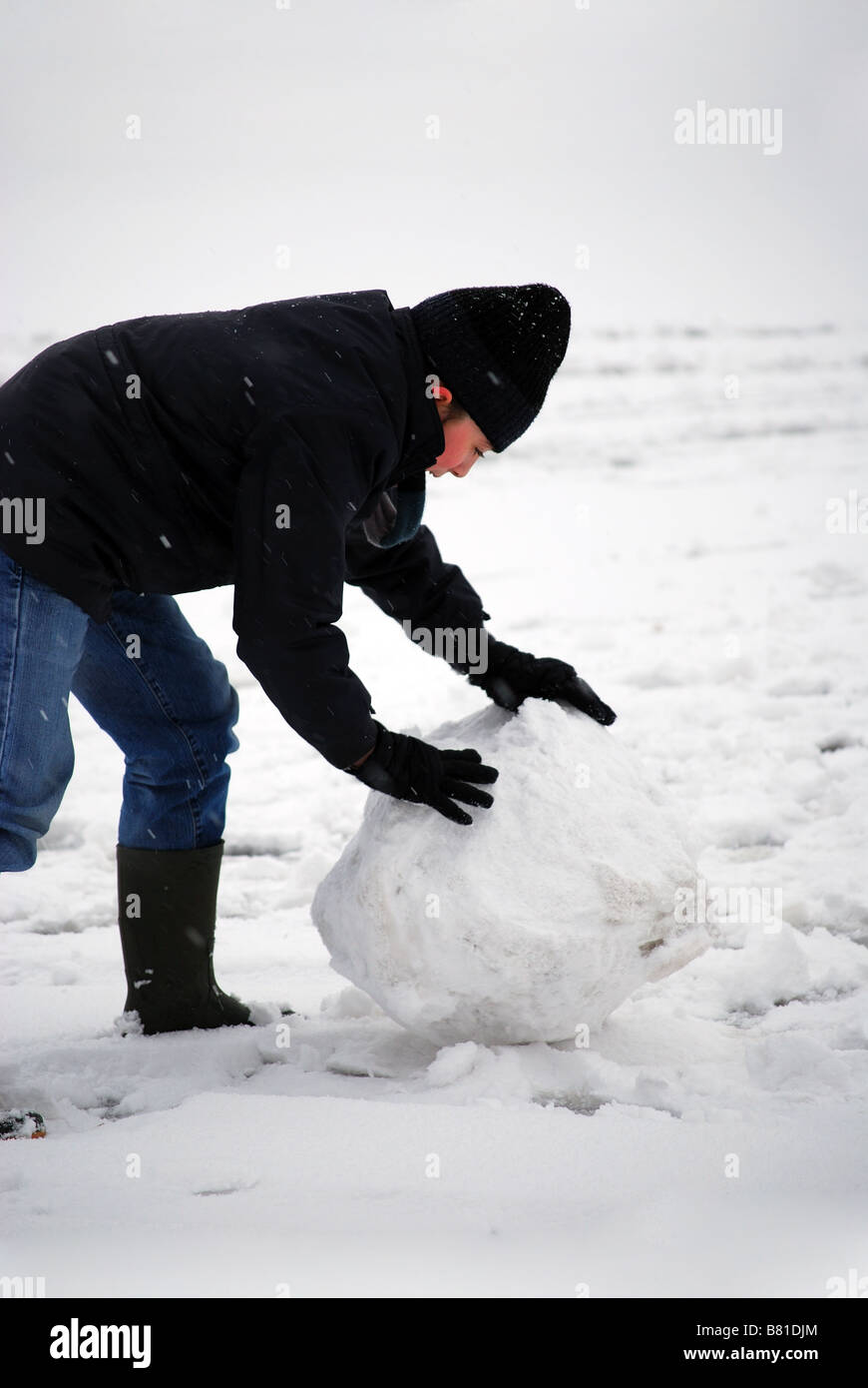 Teenager rolling a large snow ball Stock Photo - Alamy
