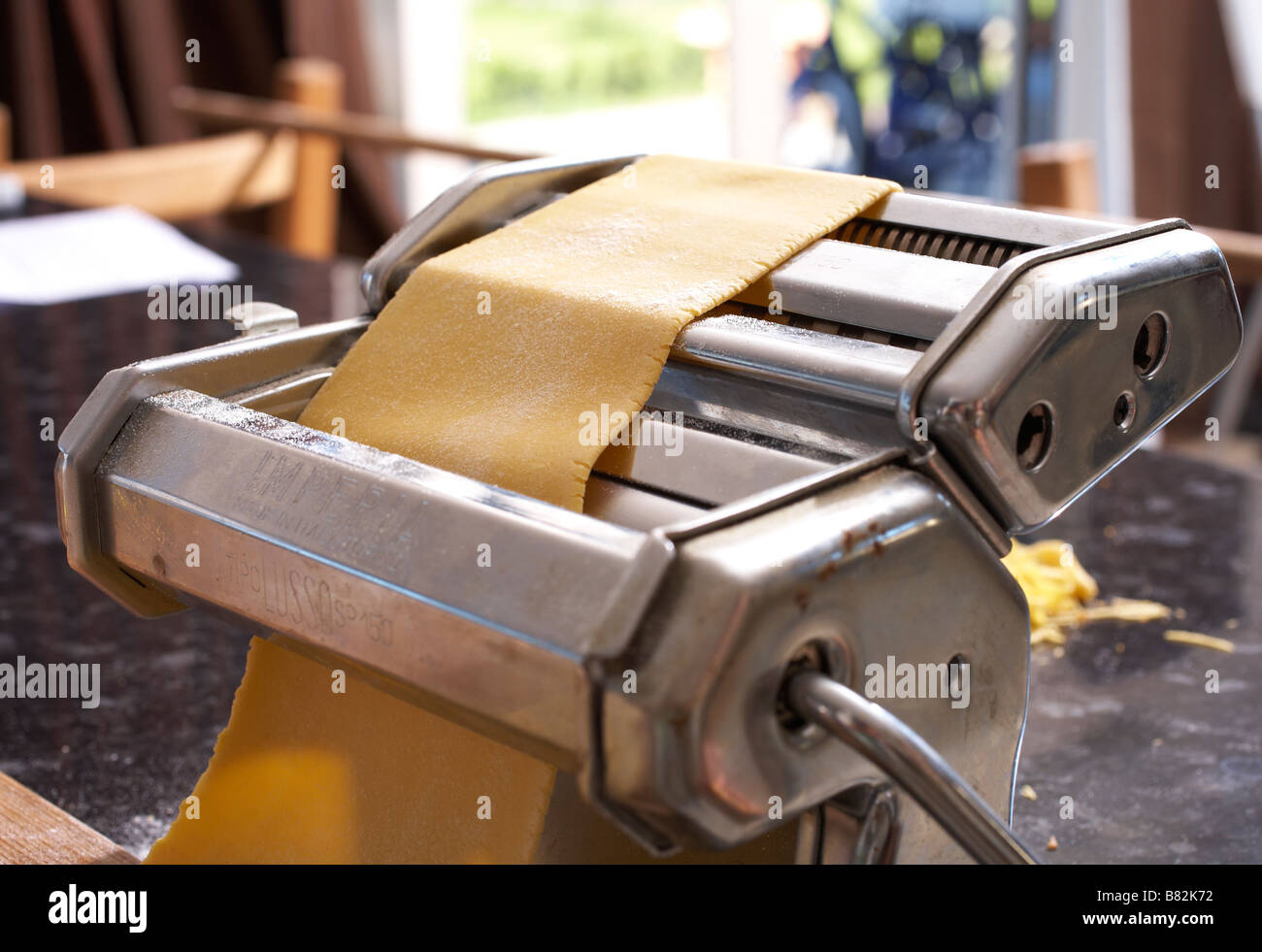 sheet of pasta being rolled through home pasta machine Stock Photo - Alamy