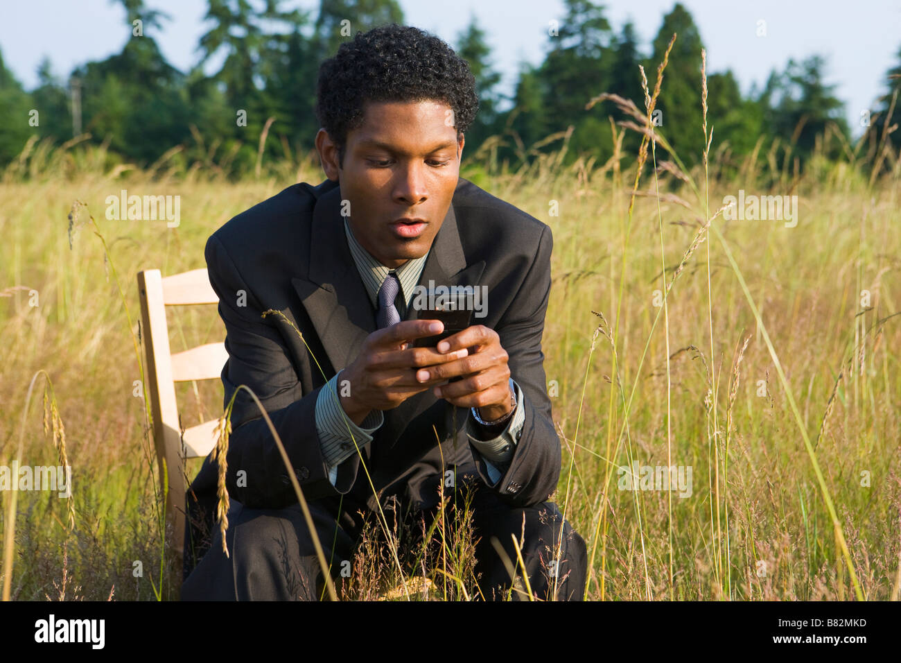 A business man sitting on a chair in a field working with his ...