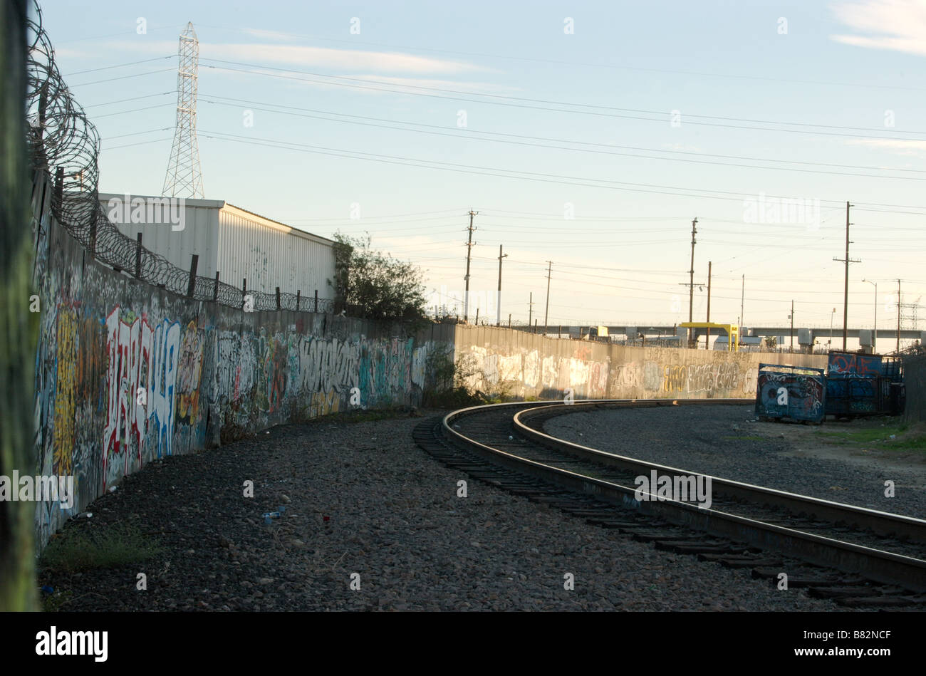 A curved stretch of rail road track running by a graffiti covered wall ...