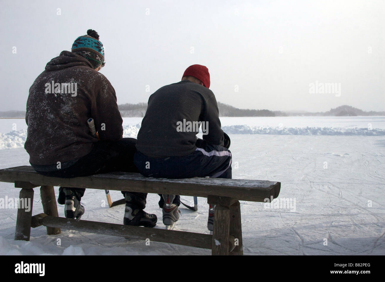 Two guys sitting on bench next to ice skating rink Stock Photo - Alamy