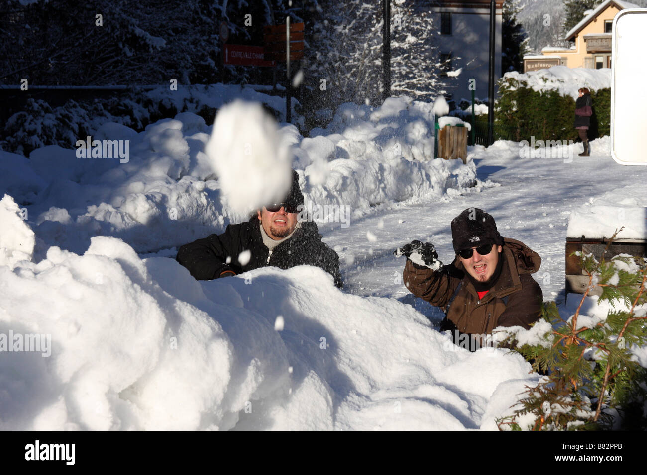 Two young men playing in the snow, hiding and throwing balls of snow at ...