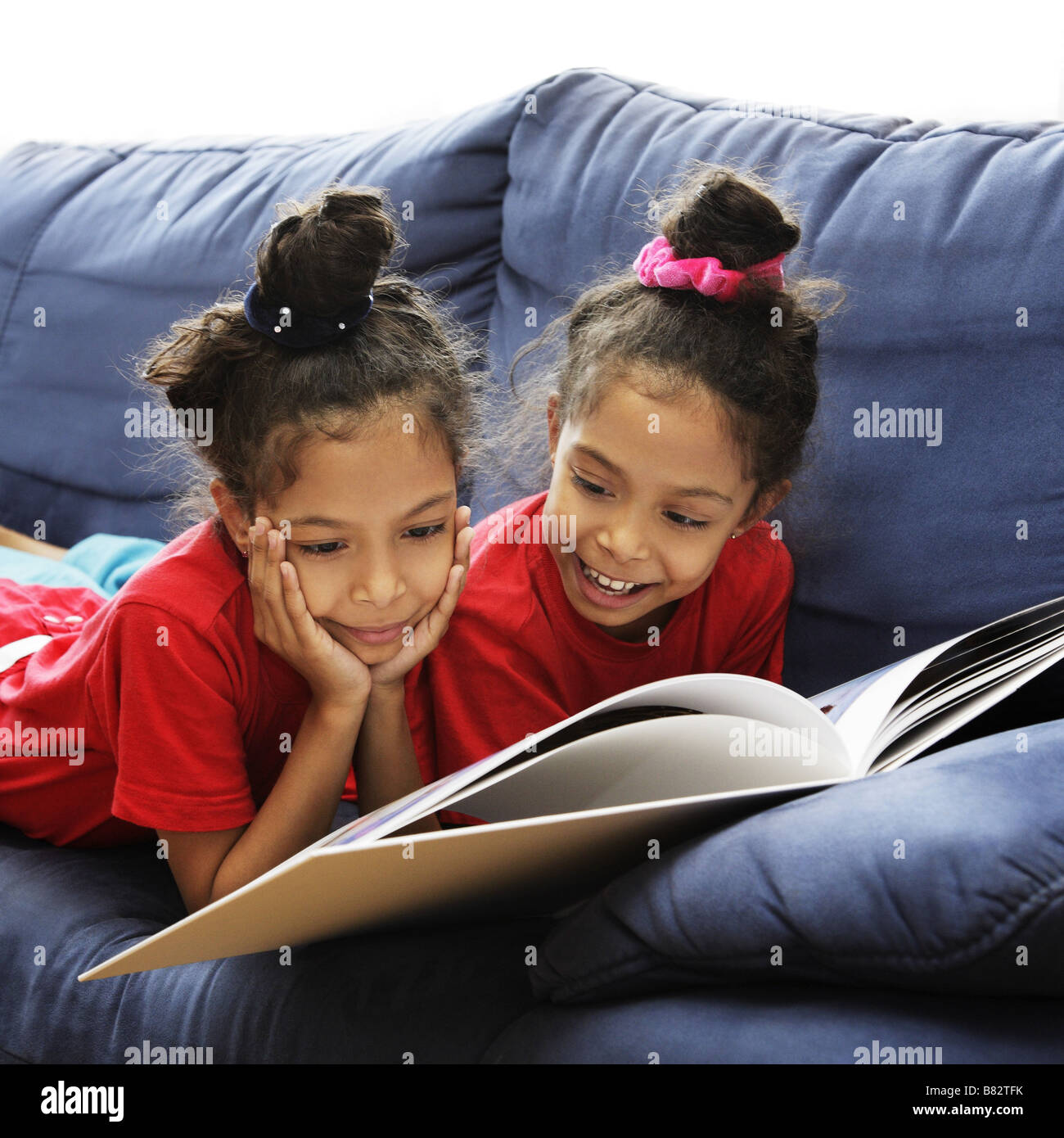 Twin sister reading a book on sofa Stock Photo - Alamy