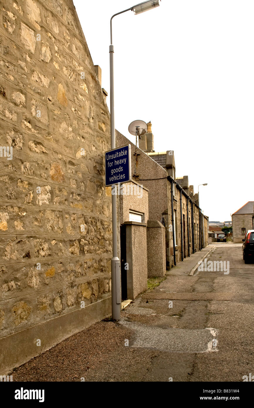 Blue sign under a streetlamp next to a stone building by a small road ...