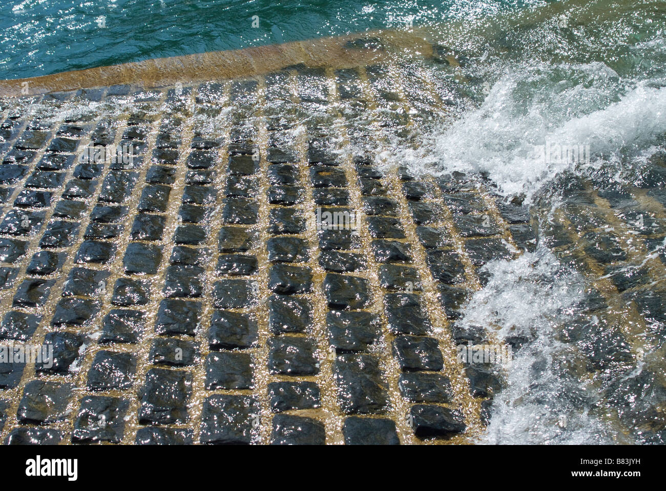 Old Harbour walkway water running over cobblestones Stock Photo - Alamy